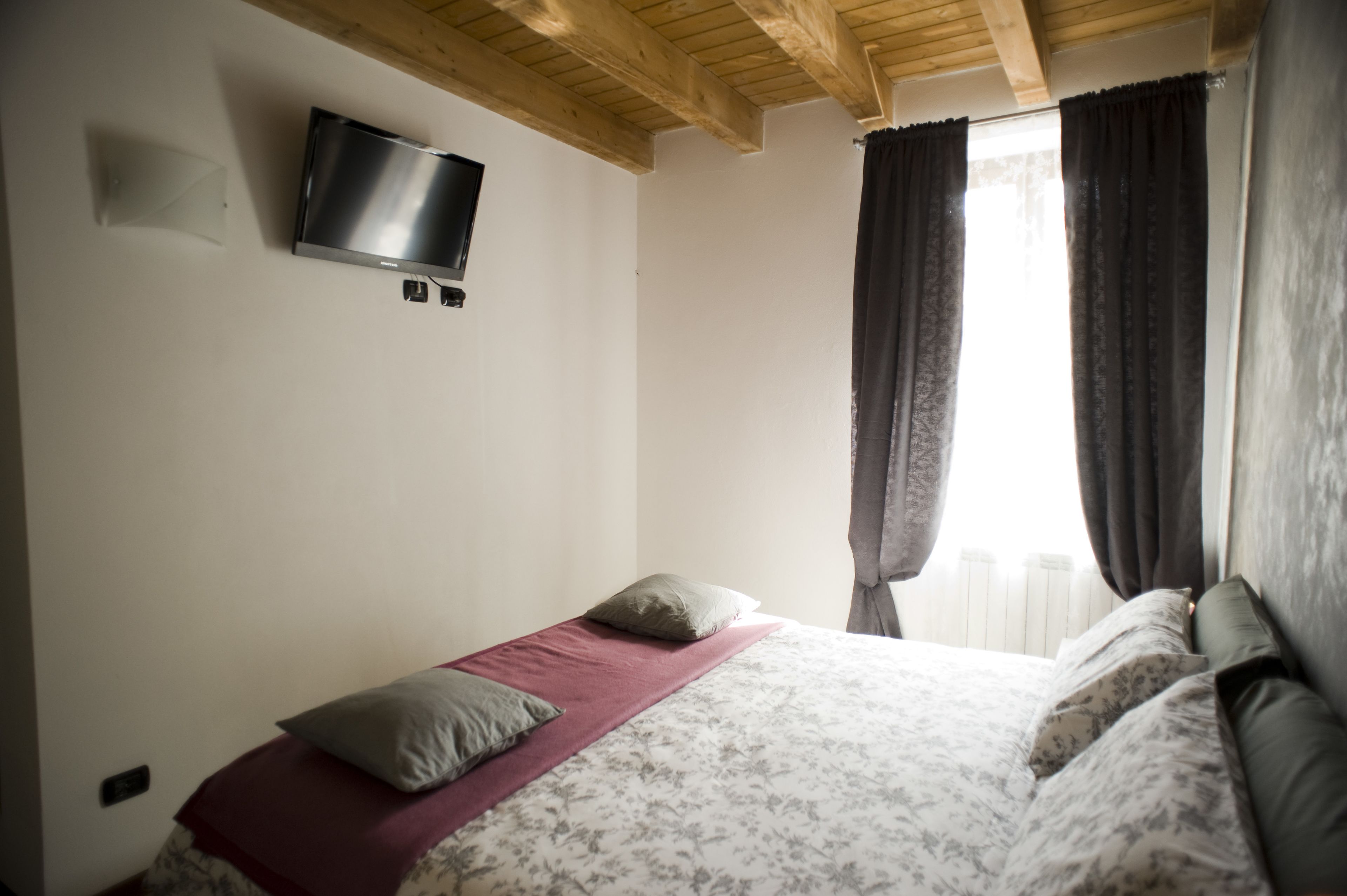Quarto com cama, televisão de tela plana na parede e janela com cortinas.