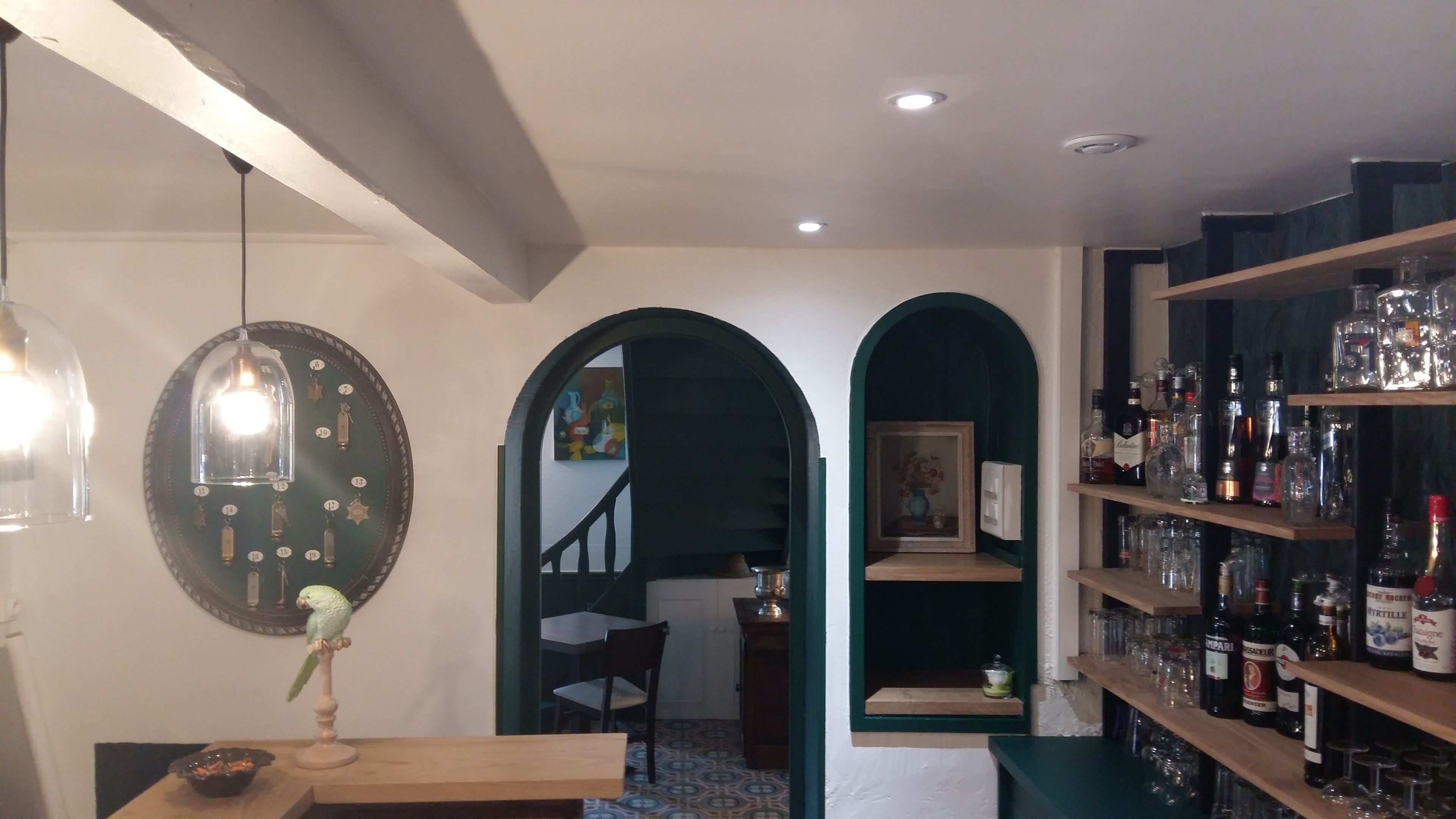 Um quarto com uma mesa de madeira, uma porta em arco verde e um relógio fixado na parede.