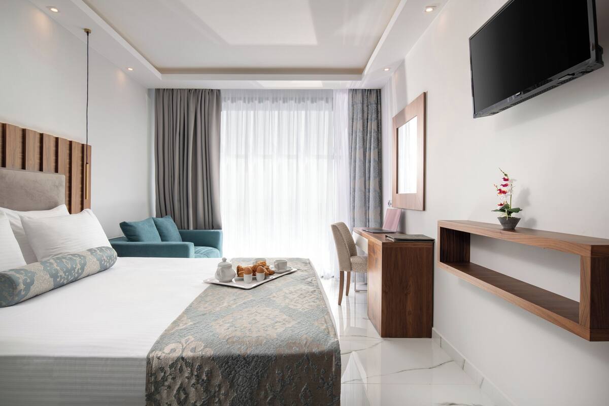 Quarto de hotel moderno com uma cama grande, uma escrivaninha, uma televisão e um espaço para sentar.