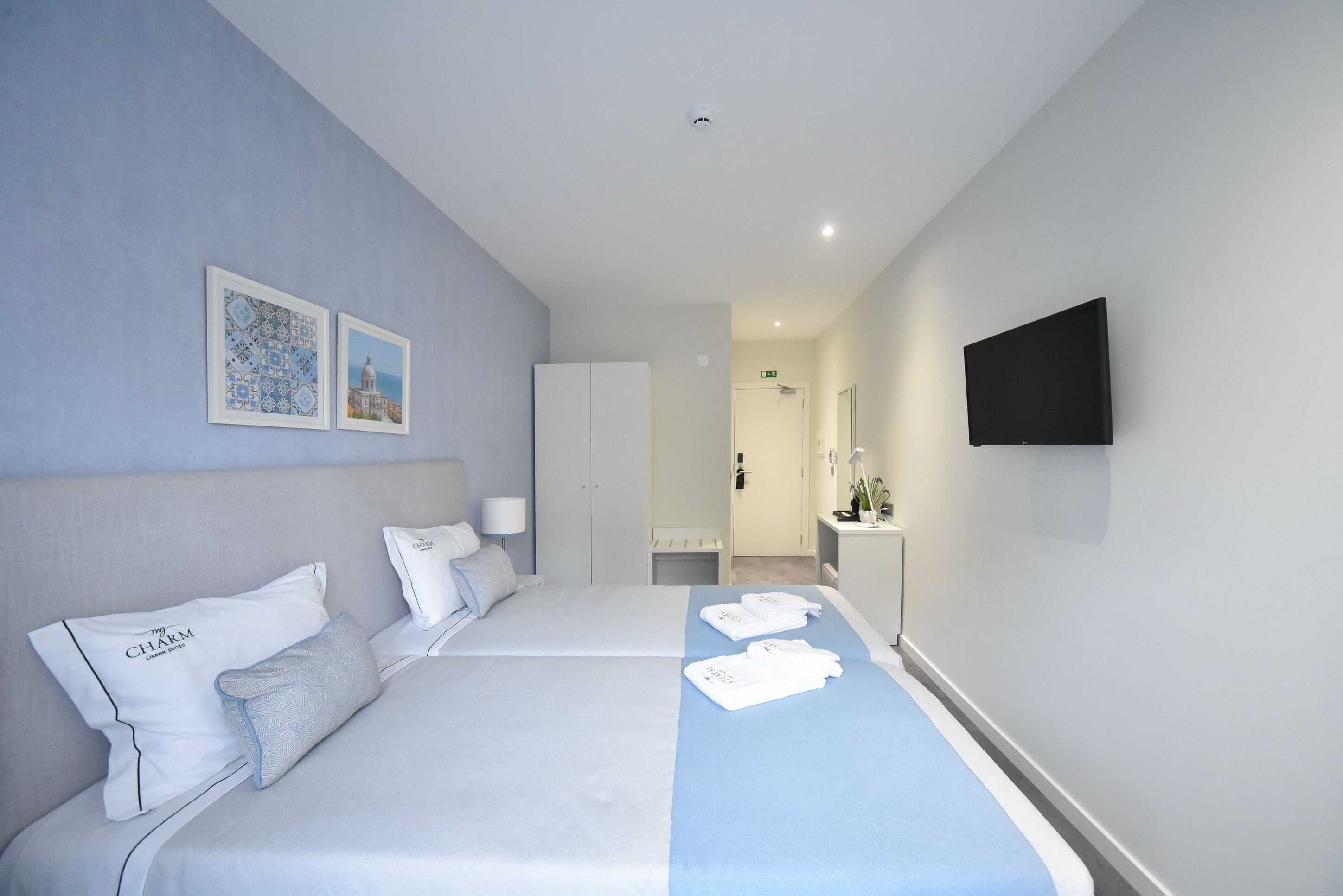 Quarto de hotel com duas camas, uma televisão de tela plana na parede e um banheiro visível ao fundo.