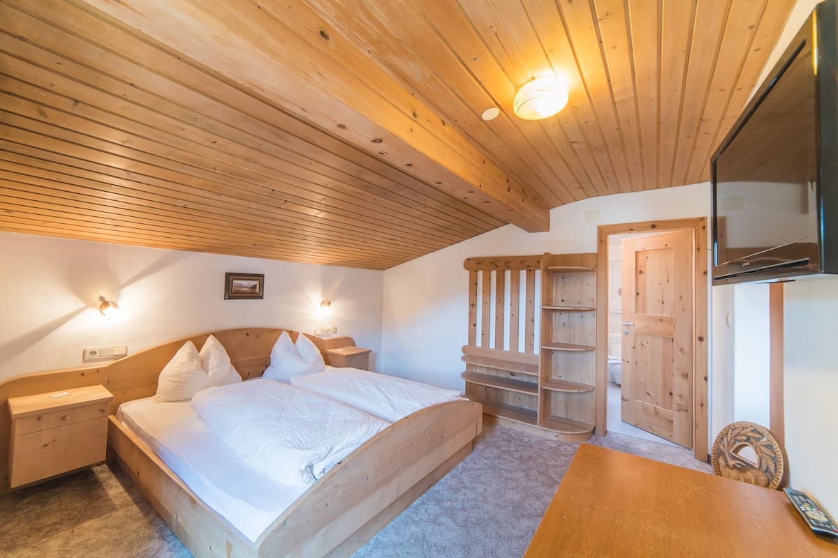 Quarto de madeira com cama, mesas de cabeceira, guarda-roupa de madeira e um espelho.