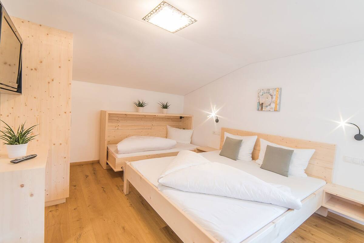 Quarto com cama de madeira, cabeceira de madeira, mesa de cabeceira, luminária na parede e uma pequena planta em vaso.