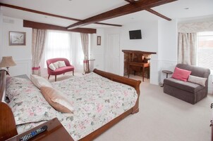 Um quarto com cama, poltrona, sofá, lareira e televisão.