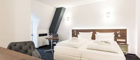 Quarto de hotel com cama, escrivaninha, cadeira e mesa pequena.