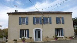 Um edifício de dois andares com telhado plano, várias janelas com persianas e uma porta central.