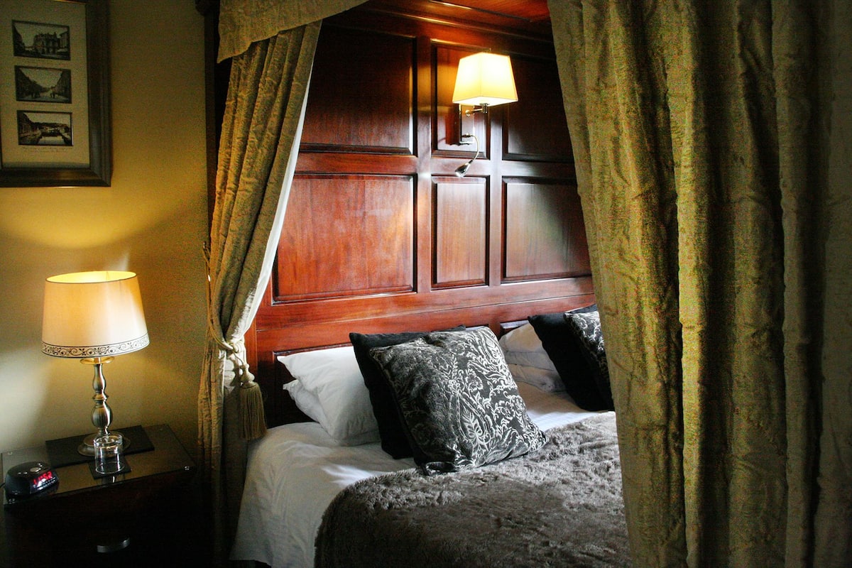 Quarto com cabeceira de madeira, luminária de cabeceira e cama com almofadas estampadas.