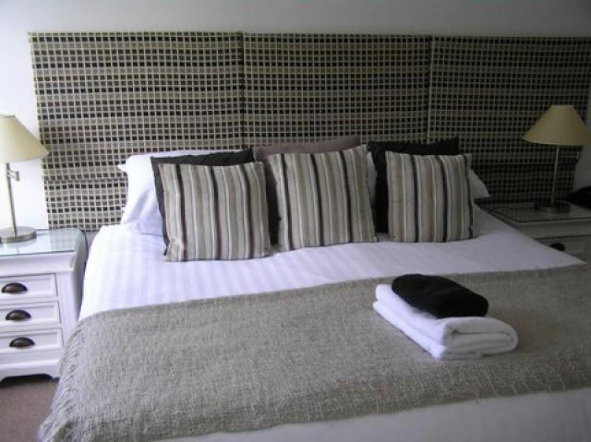 Cama bem arrumada com travesseiros listrados, um cobertor cinza e uma toalha dobrada.