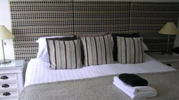 Cama bem arrumada com travesseiros listrados, um cobertor cinza e uma toalha dobrada.