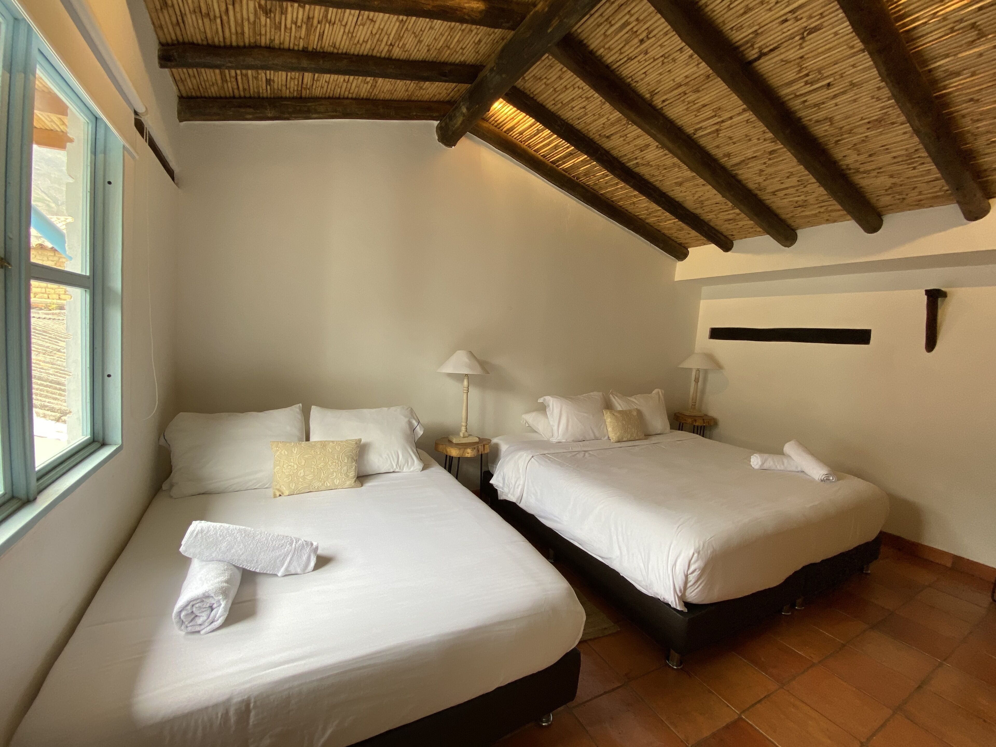 Quarto com duas camas, cada uma com roupa de cama e almofadas brancas, uma janela e teto de madeira.