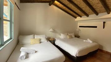 Quarto com duas camas, cada uma com roupa de cama e almofadas brancas, uma janela e teto de madeira.