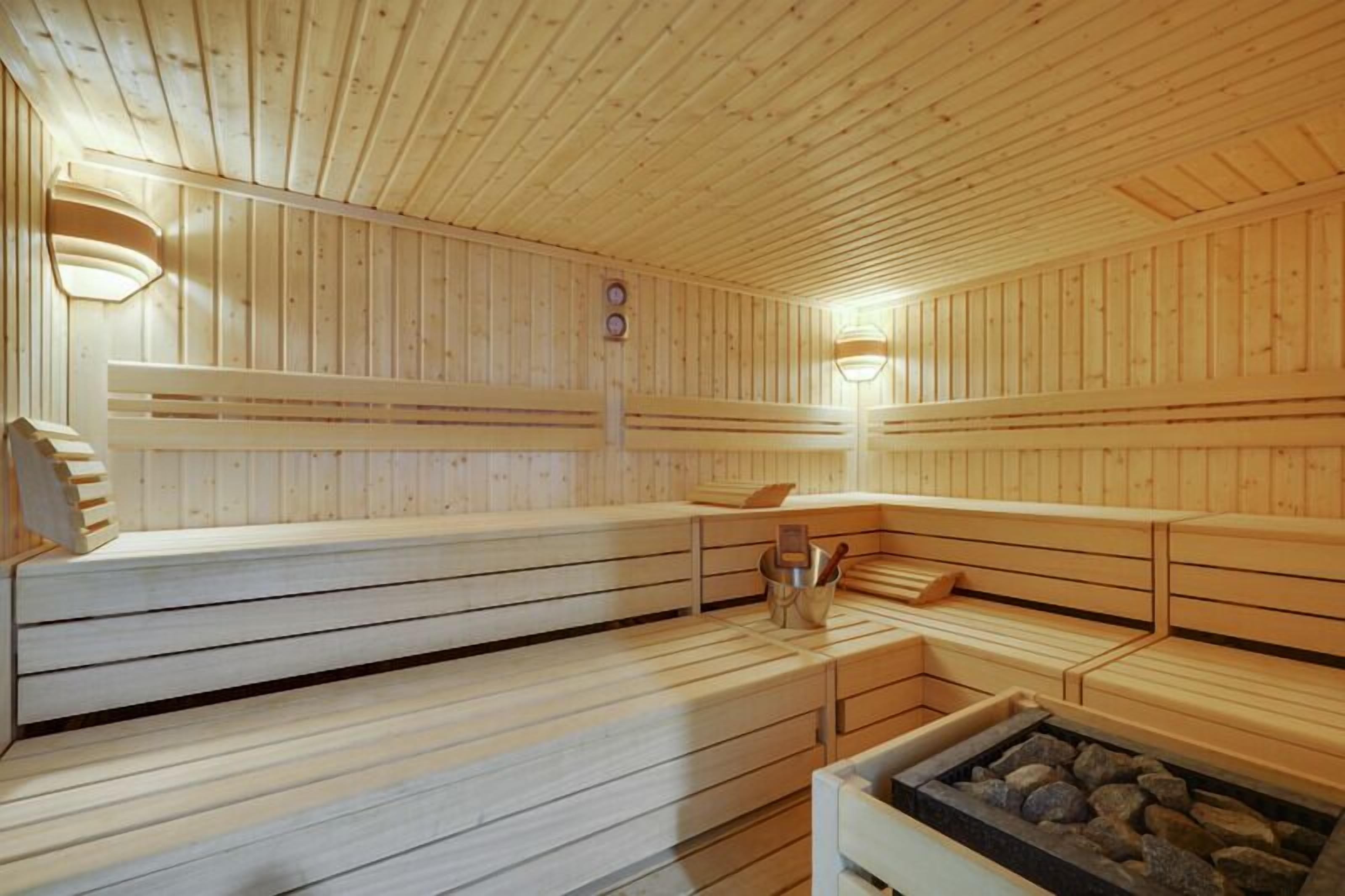 Uma sauna com bancos de madeira, um aquecedor fixado na parede e uma bacia com pedras.