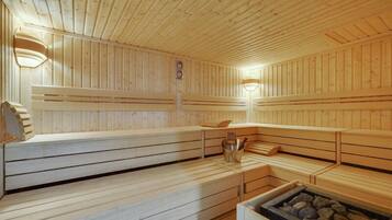 Uma sauna com bancos de madeira, um aquecedor fixado na parede e uma bacia com pedras.