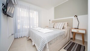 Quarto com cama, mesa de cabeceira, luminária e televisão na parede.