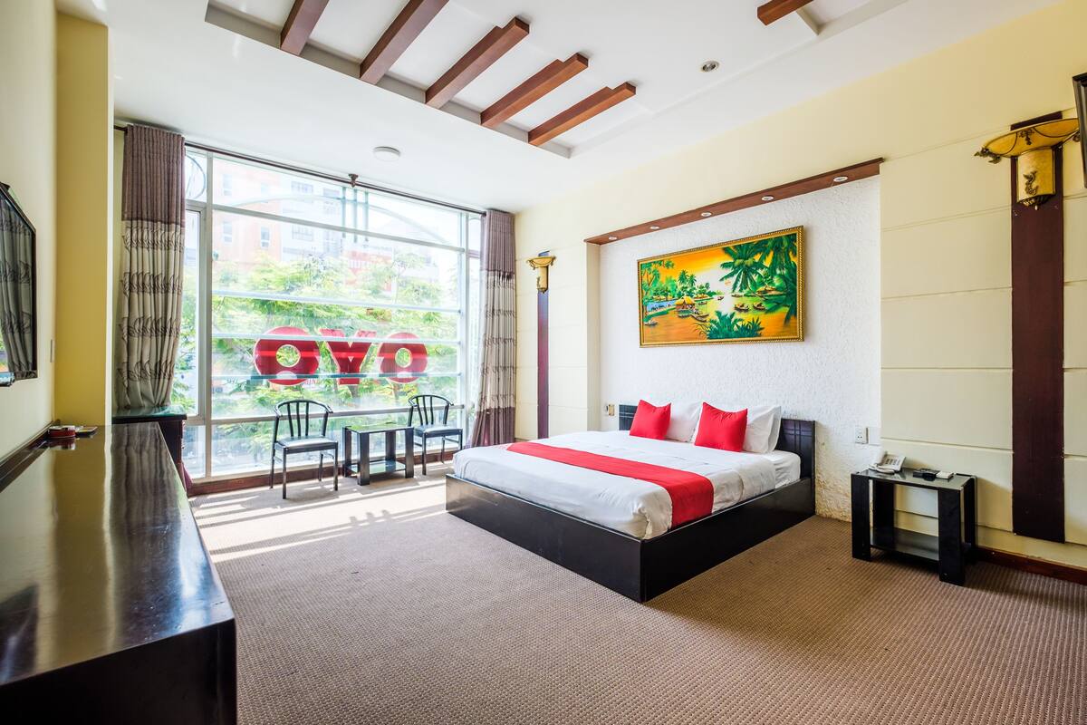 Quarto de hotel com uma cama grande, uma escrivaninha, uma cadeira e uma janela com vista para o verde.