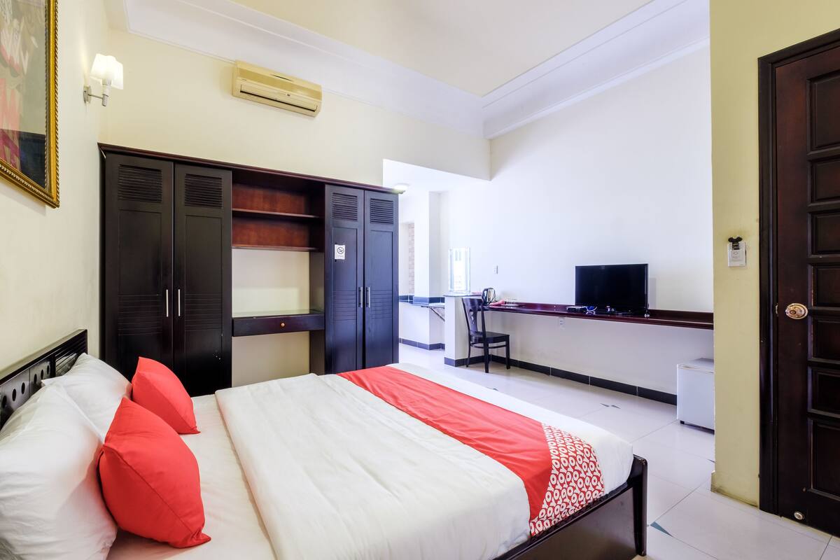 Quarto de hotel com cama, escrivaninha, televisão e armário.