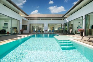 Uma área de piscina moderna com água azul cristalina, espreguiçadeiras e portas de vidro que dão para um edifício.