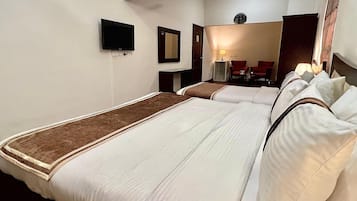 Quarto de hotel com uma cama grande, uma televisão de tela plana na parede, uma mesa com cadeira e um relógio na parede.