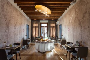 Uma sala de jantar com uma mesa redonda posta para uma refeição, vigas de madeira no teto e vista do exterior pela janela.