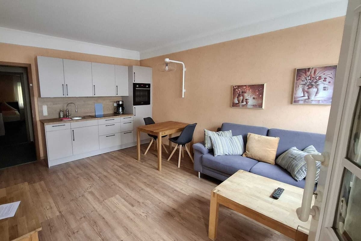 Um espaço compacto com cozinha americana, área de refeições e sala de estar com sofá e mesa.