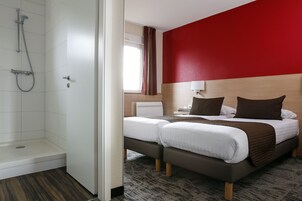 Quarto de hotel com chuveiro, duas camas, uma parede de destaque vermelha e uma janela com cortinas.