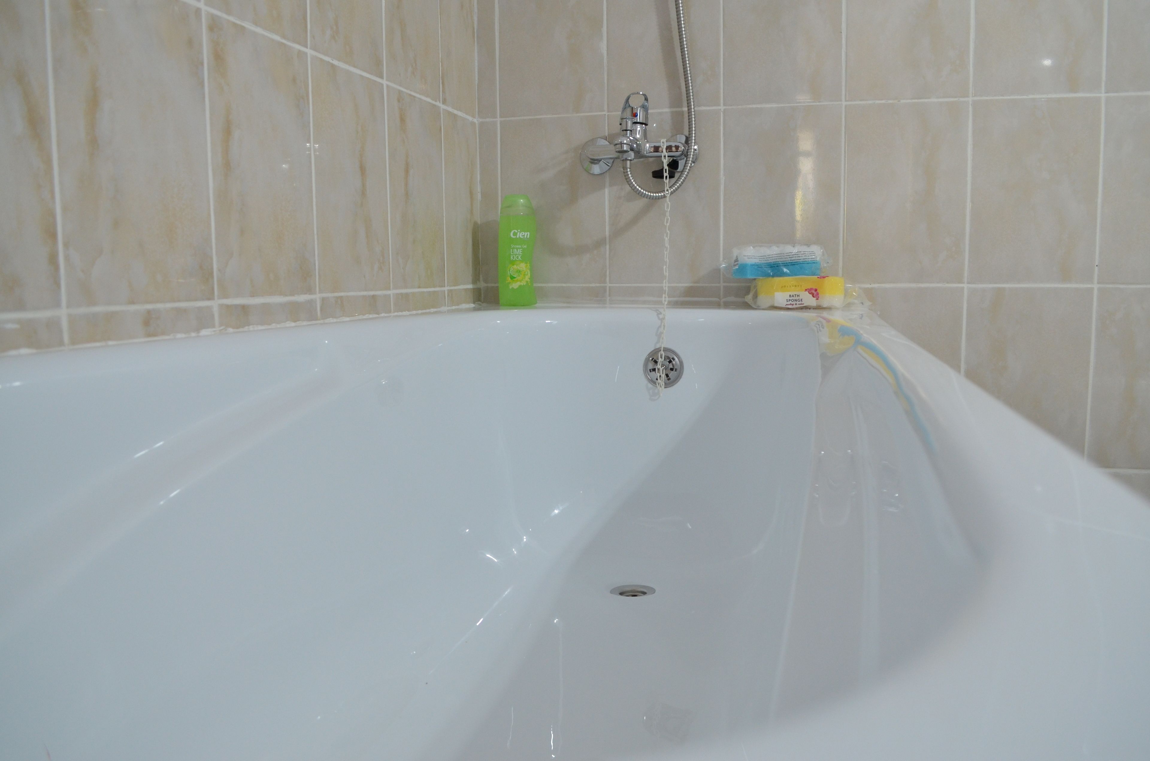 Uma banheira com chuveiro, uma garrafa de shampoo Cien e um sabonete.