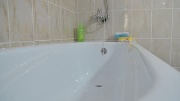 Uma banheira com chuveiro, uma garrafa de shampoo Cien e um sabonete.