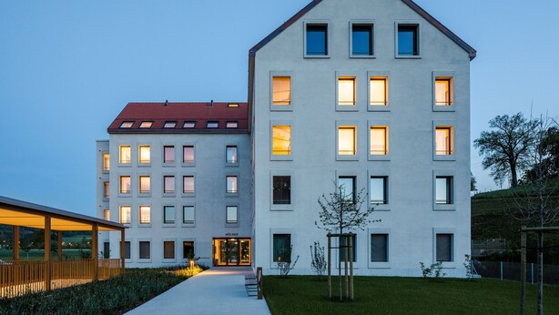 Um edifício moderno de vários andares com telhado plano e uma combinação de janelas retangulares e quadradas.