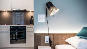 Cozinha moderna com forno embutido e um pequeno espaço para refeições. Há uma mesa de cabeceira com uma luminária, uma tomada e um painel de parede de madeira.