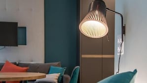 Quarto de hotel moderno com cama, escrivaninha, sofá e televisão fixada na parede.