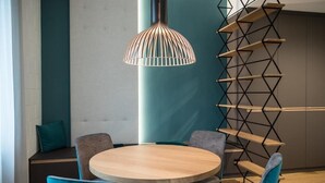 Uma área de jantar moderna com uma mesa redonda de madeira, cadeiras estofadas em azul, uma estante geométrica singular e uma luminária pendente com design em relevo.