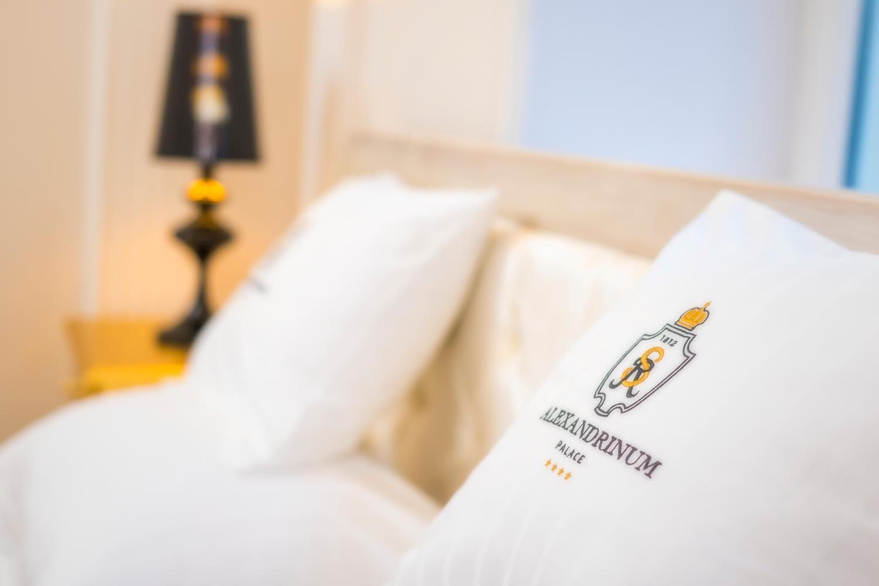 Uma cama com almofadas exibindo o logotipo do Alexandrium Palace.
