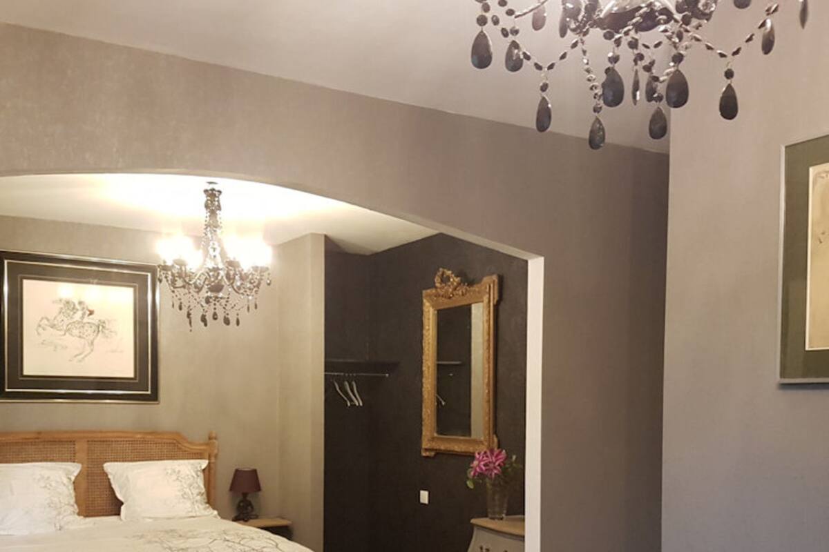 Quarto com uma cama grande, um banco de madeira, cômoda, espelho e lustre.