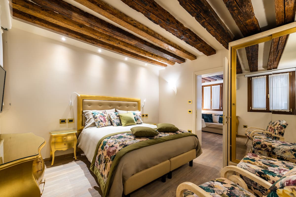 Quarto com cama, mesas de cabeceira, uma cadeira e teto de madeira.