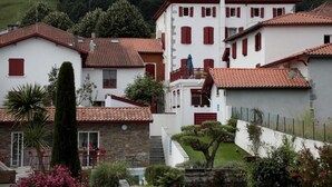 Área residencial com casas de telhado vermelho e paredes brancas, cercada por vegetação e um morro.