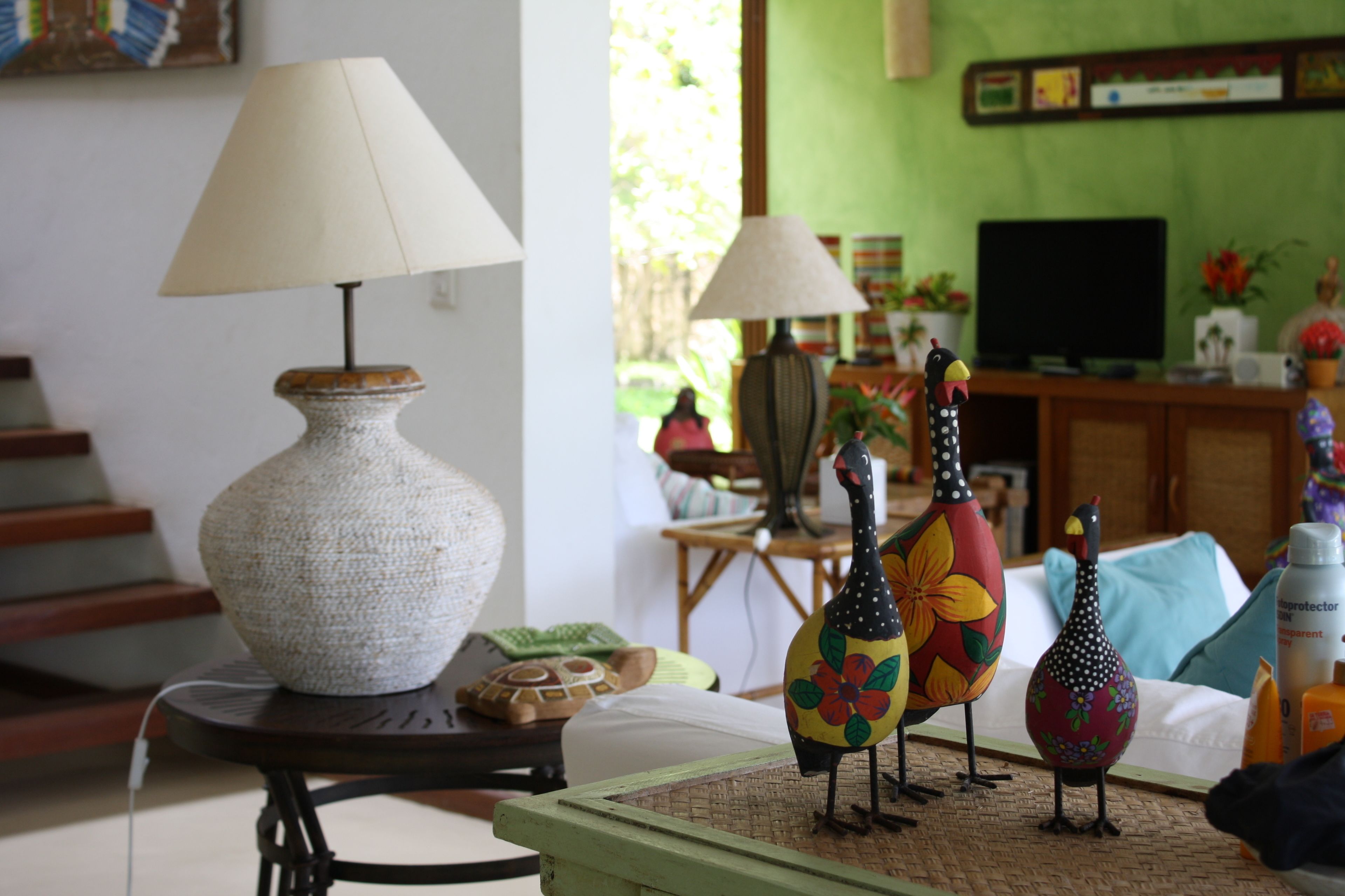Uma sala de estar com uma luminária, um vaso e pássaros decorativos sobre uma mesa.