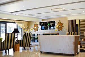 Um saguão de hotel com balcão de recepção, cadeiras listradas, um sofá e arte decorativa na parede.