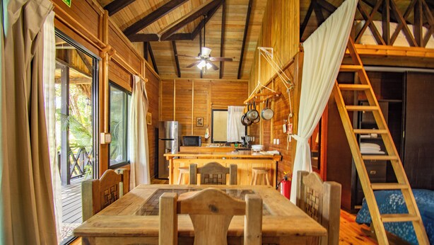 Interior de madeira com mesa de jantar, cadeiras, cozinha e escada.