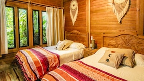 Quarto de cabana de madeira com duas camas, uma janela com cortinas e um objeto pendurado na parede.