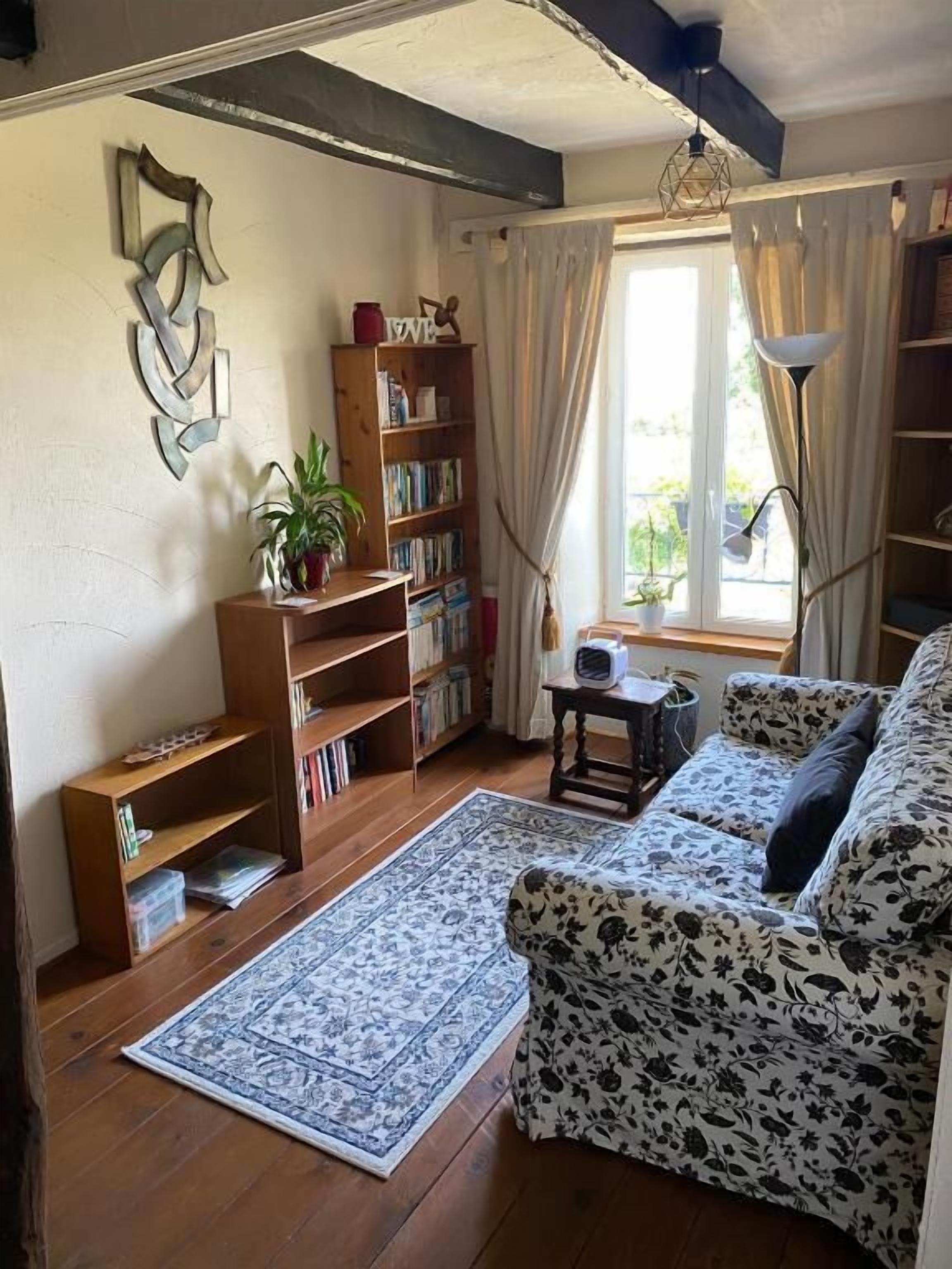 Uma sala de estar aconchegante com um sofá, estante de livros, tapete e janela com cortinas.