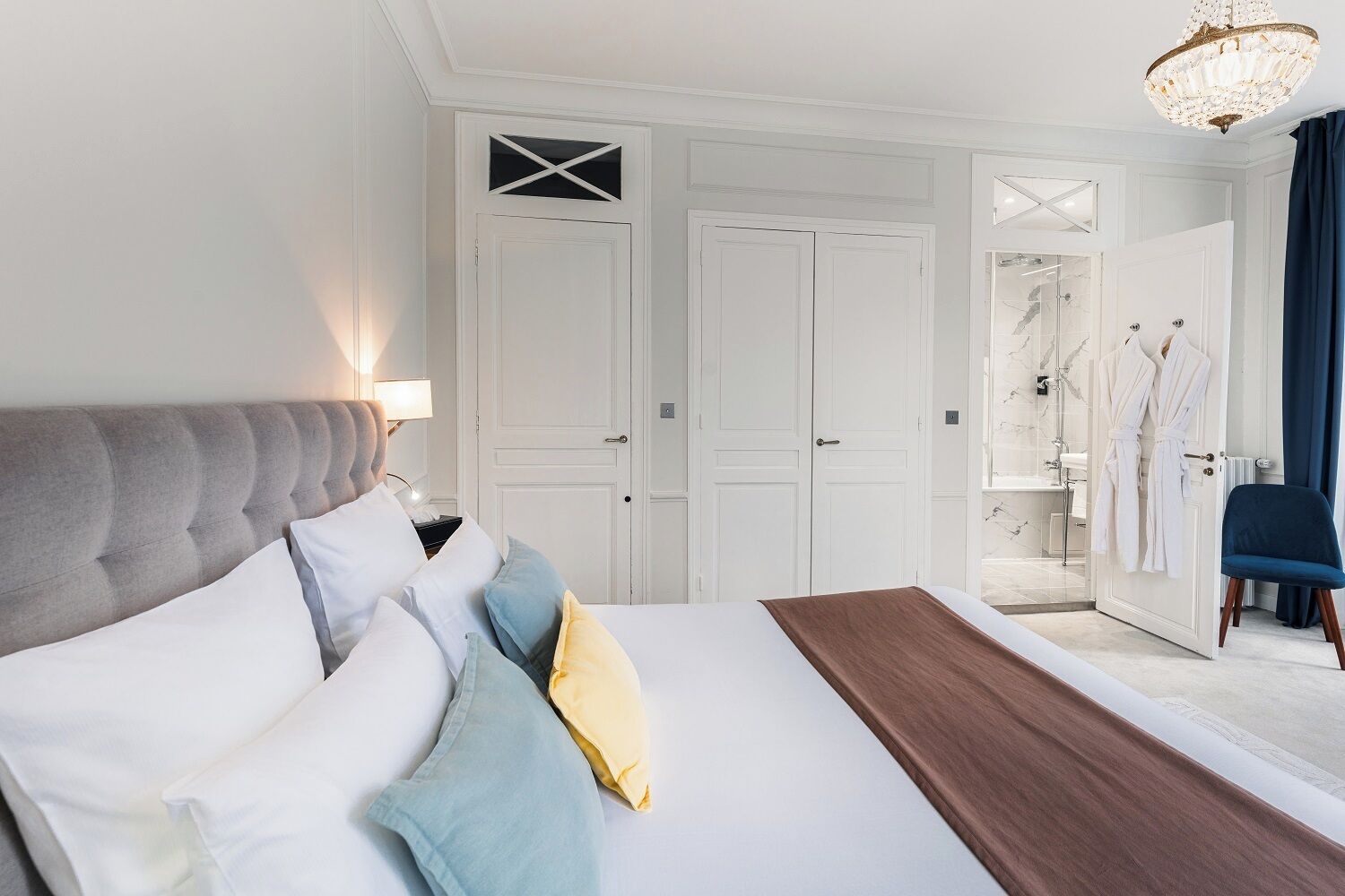 Quarto de hotel com uma cama grande, cabeceira de madeira e vista para o banheiro através de uma porta aberta.