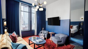 Quarto de hotel moderno com sofá, poltronas, mesa de centro, uma guitarra e uma TV.