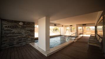 Uma área de spa com parede de pedra, piso de madeira, piscina e áreas de estar.