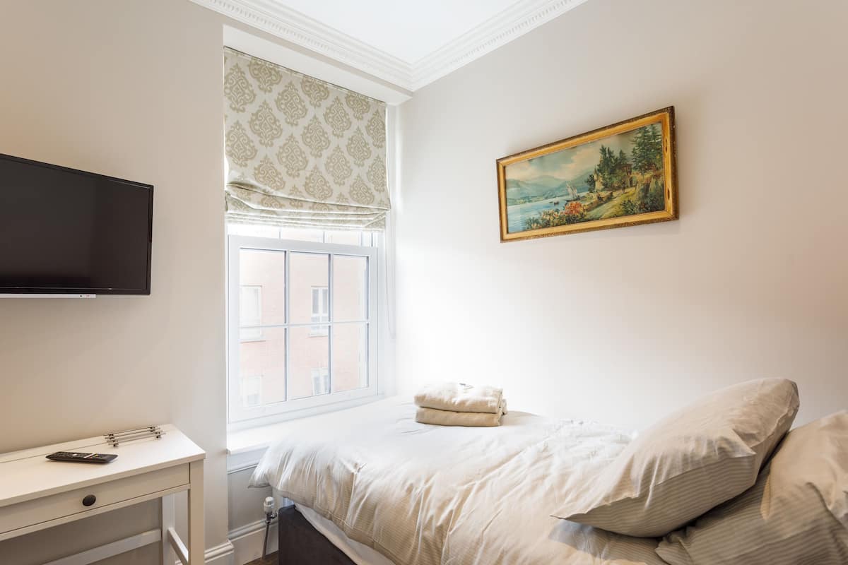 Quarto com cama, televisão, escrivaninha e janela com cortinas estampadas.