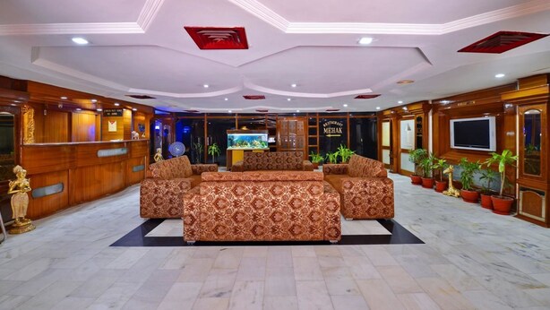 Um saguão de hotel com balcão de recepção, sofás estampados, uma televisão e plantas em vasos.