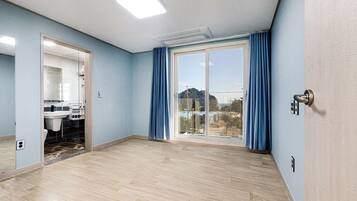 Um quarto espaçoso com uma grande porta de vidro deslizante para uma varanda, uma pia embutida e um chão de madeira clara.