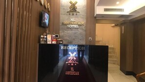 Uma área de recepção com painel de parede em madeira, uma televisão montada e um balcão de recepção com tapete vermelho.