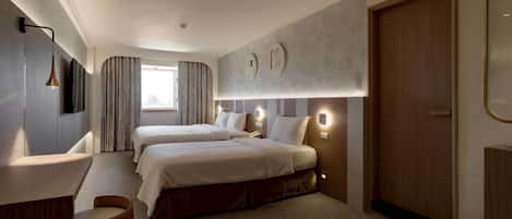 Quarto de hotel com duas camas, uma escrivaninha, uma cadeira, uma televisão e uma porta.