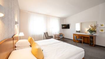 Quarto de hotel com cama, escrivaninha, cadeira, televisão e janela com cortinas.