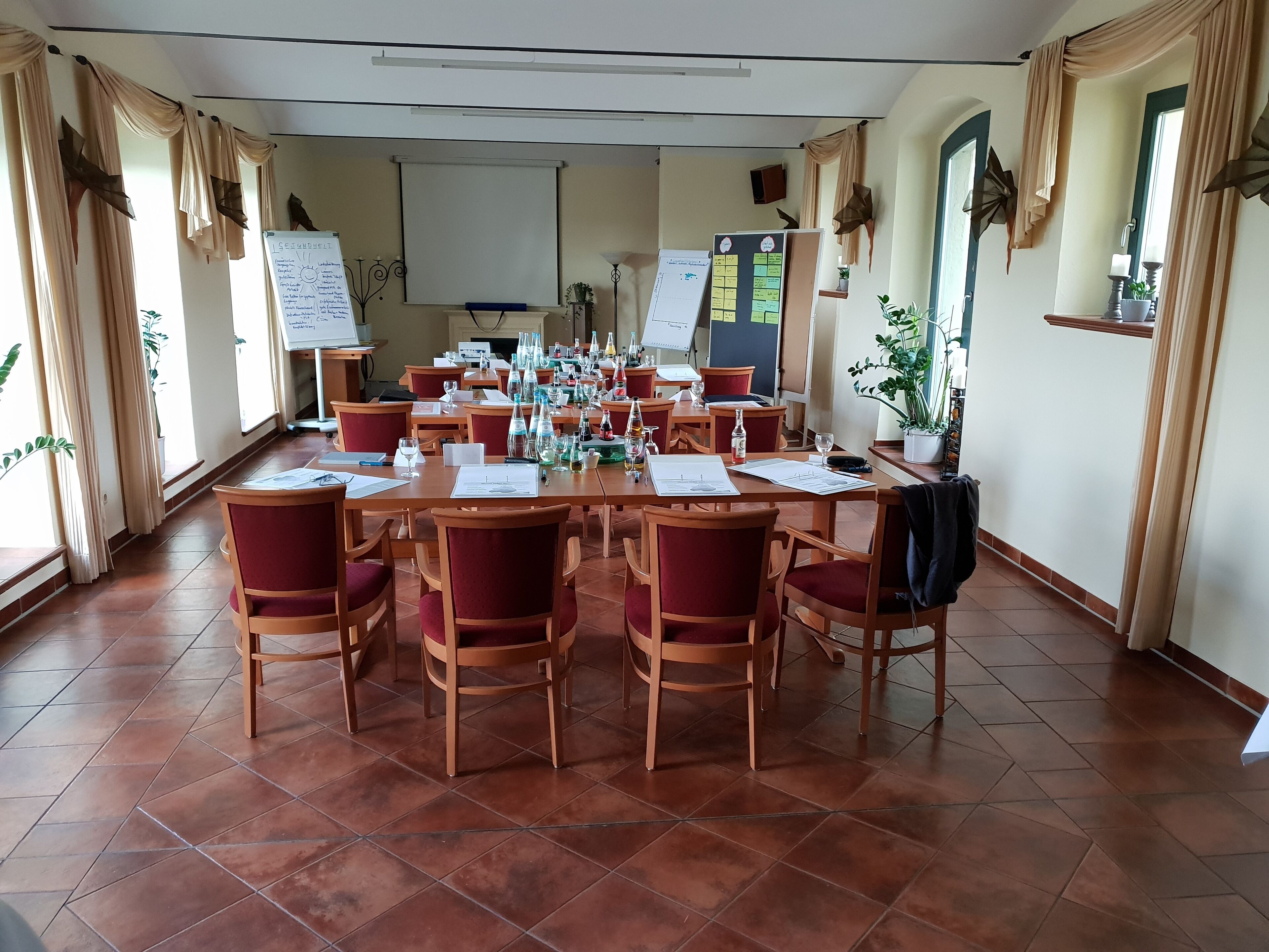 Uma sala de conferências com uma mesa comprida, cadeiras vermelhas e um quadro branco.