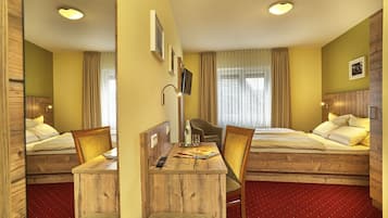 Quarto de hotel com duas camas, uma escrivaninha de madeira com cadeira, um espelho e um tapete vermelho.